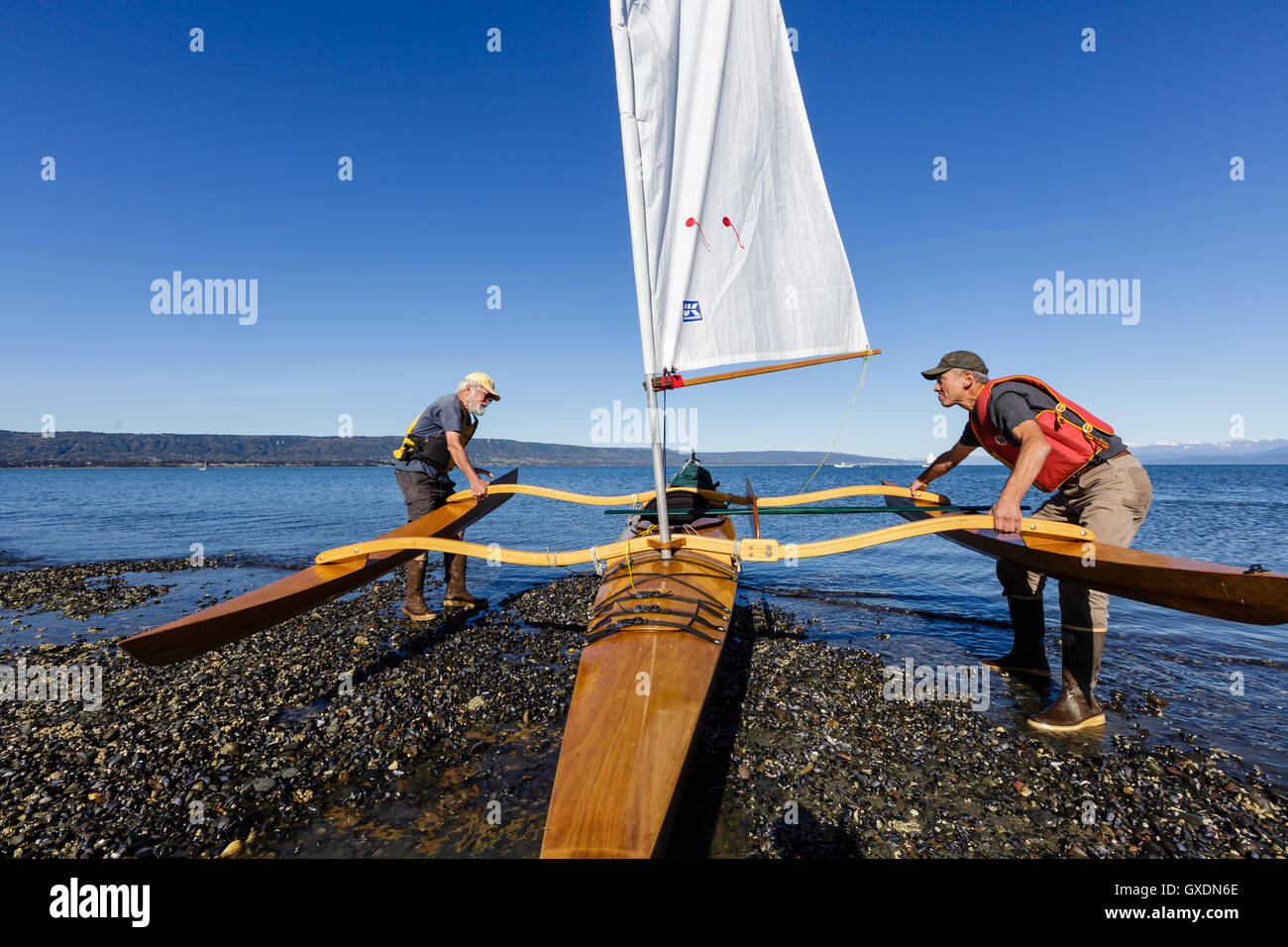 Two men carry their wooden boat into the water Stock Photo - Alamy