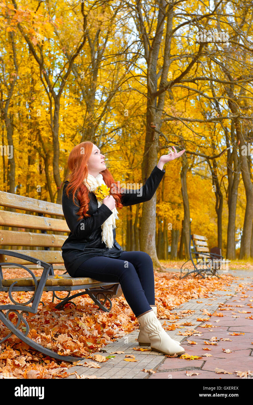 girl in fall season, sit on bench in city park, yellow trees and fallen ...