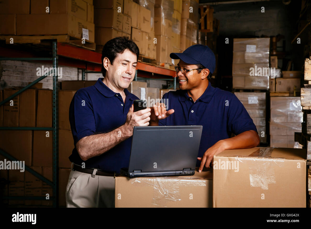 Warehouse workers using laptop and cell phone Stock Photo - Alamy