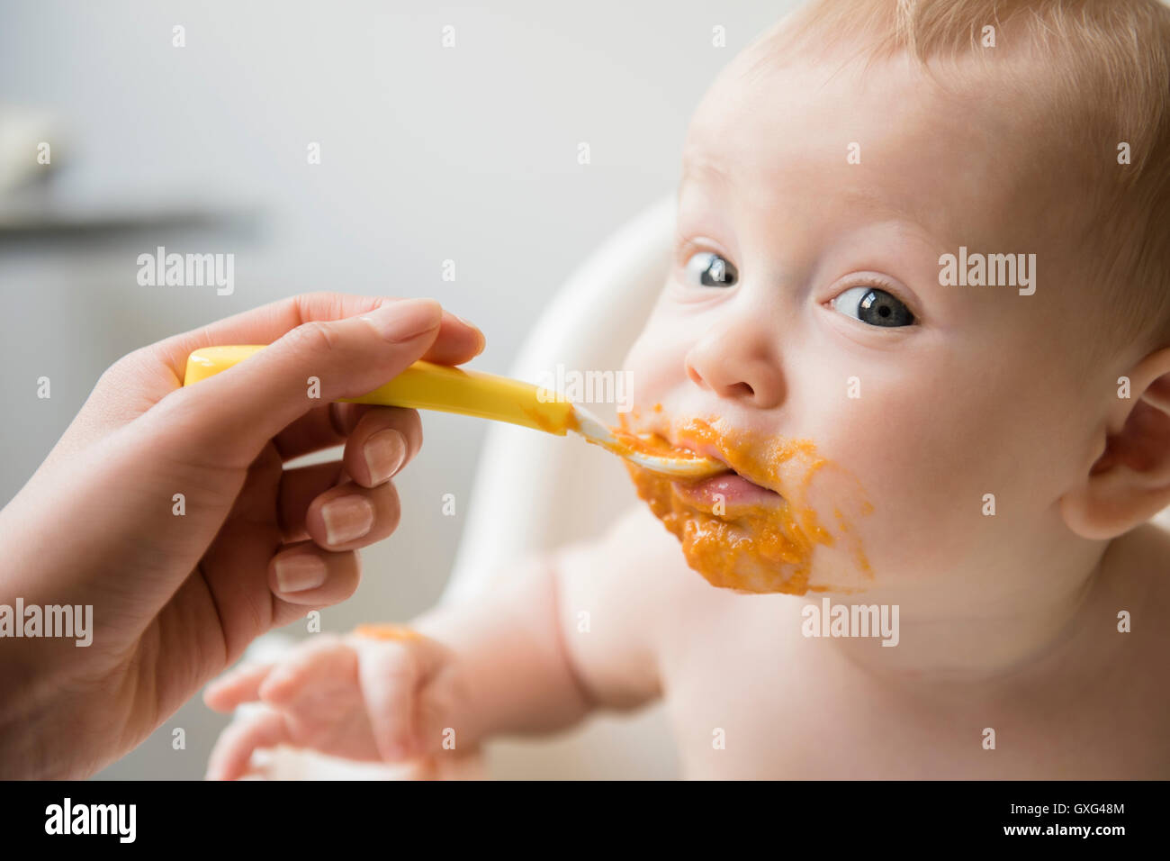 Mother feeding messy baby son with spoon in high chair Stock Photo - Alamy