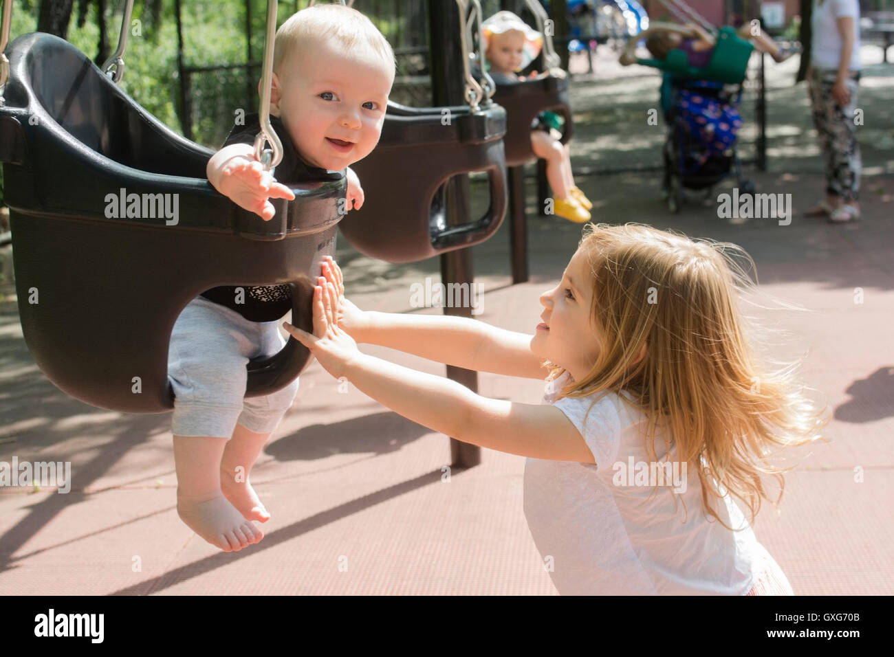 Caucasian girl pushing baby in swing Stock Photo - Alamy