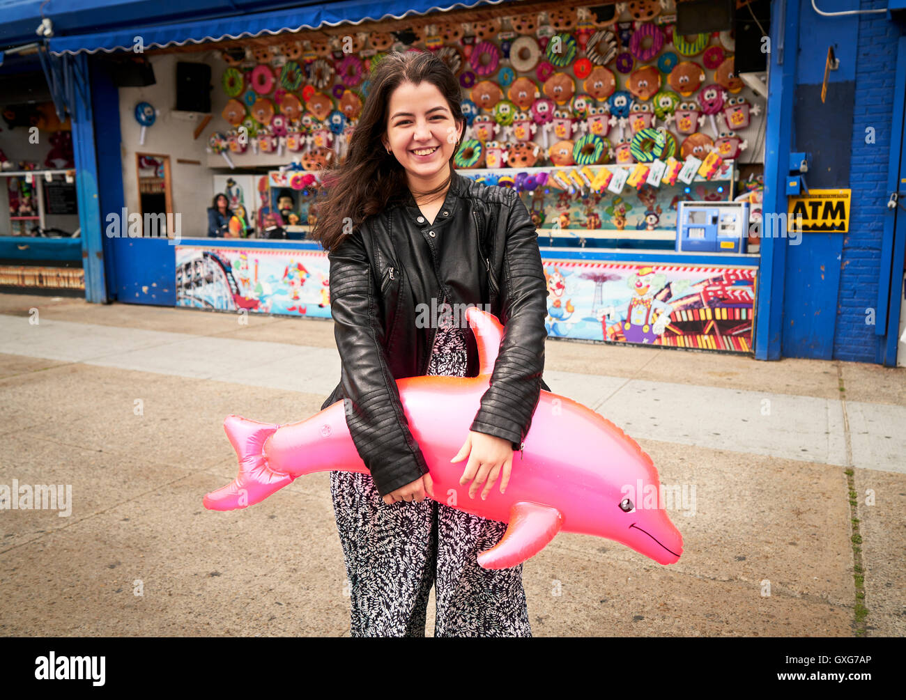 Mixed Race woman holding pink inflatable dolphin at amusement park ...