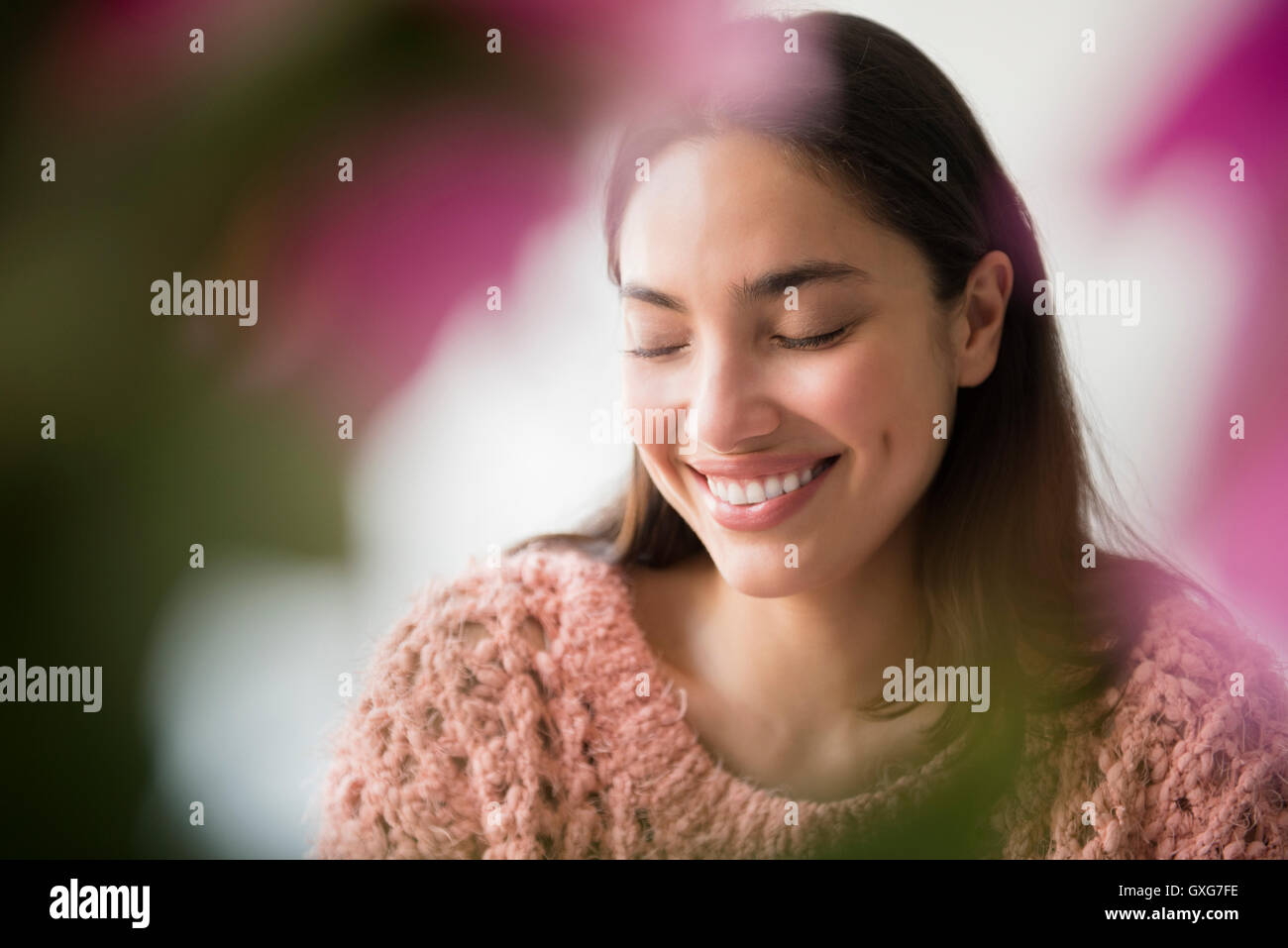 Hispanic woman smiling behind pink flowers Stock Photo - Alamy