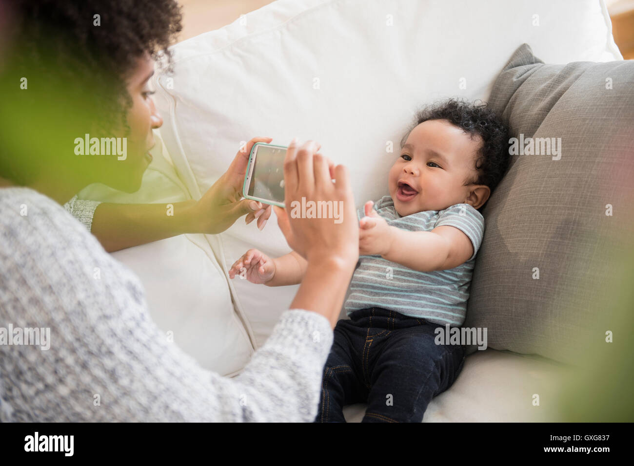 Mother photographing baby son with cell phone on sofa Stock Photo - Alamy