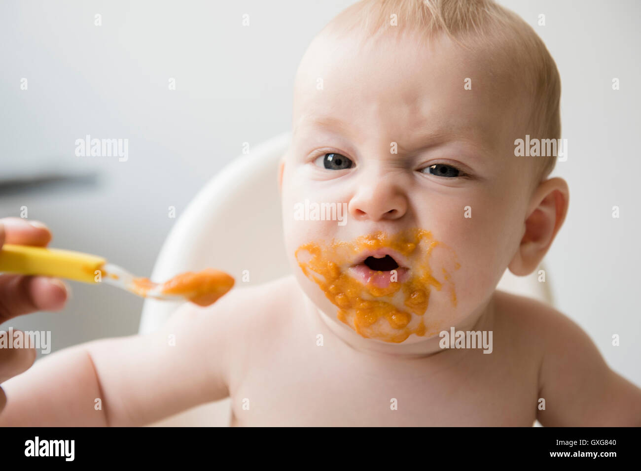 Mother feeding messy baby son with spoon in high chair Stock Photo - Alamy