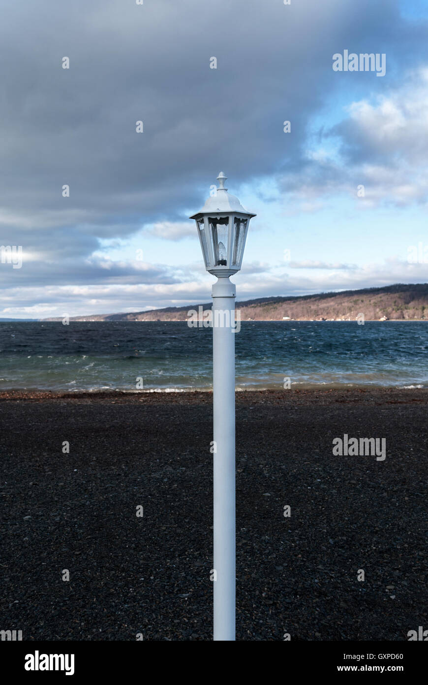 A single lamp post is centered in frmae on a beach. The beach is pebble ...