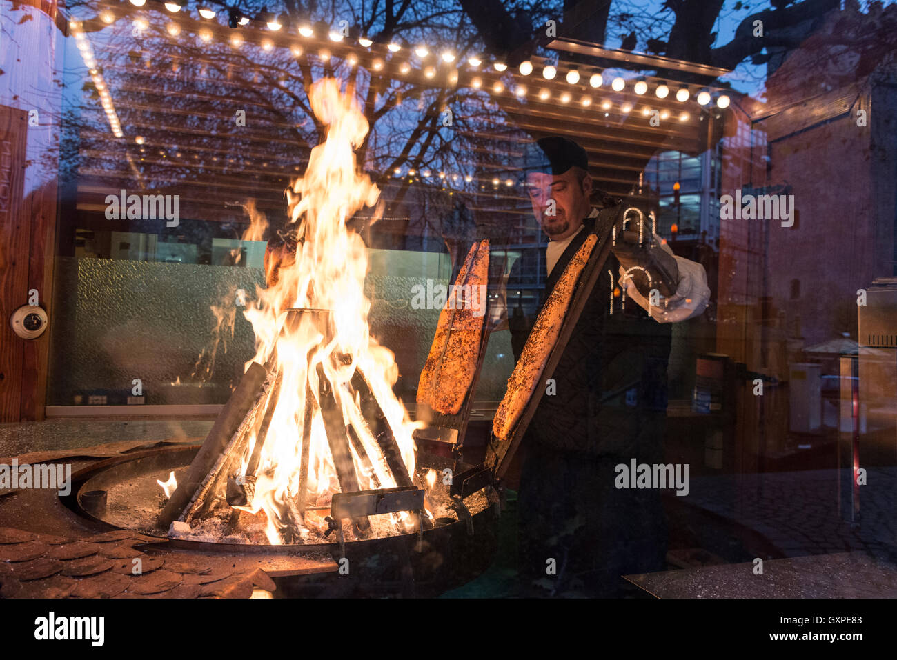 A stall holder tending to his smoked salmon being cooked by a log fire ...