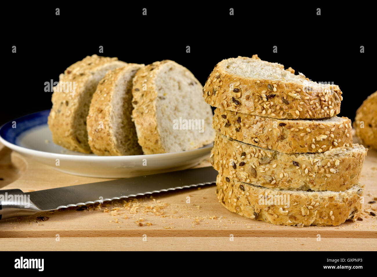 Sliced granary baguette on chopping board, against a black background ...