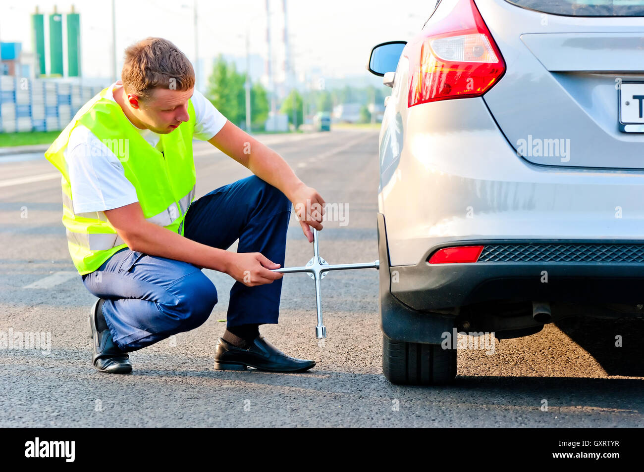 mechanic in a vest tie the wheel to the car on the road Stock Photo - Alamy