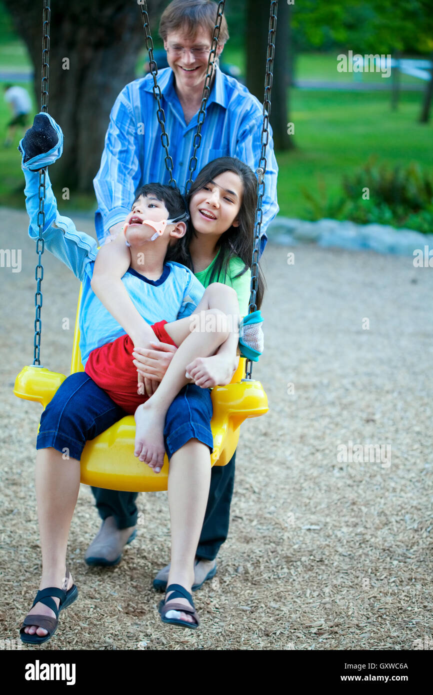 Big sister holding disabled brother on special needs swing at pl Stock ...