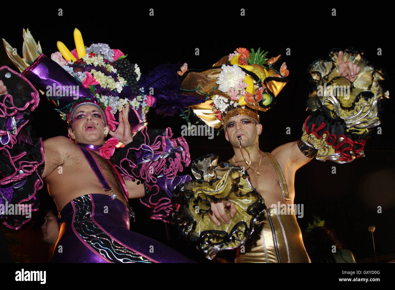 Two shirtless men in colorful costumes dance on a float during a ...