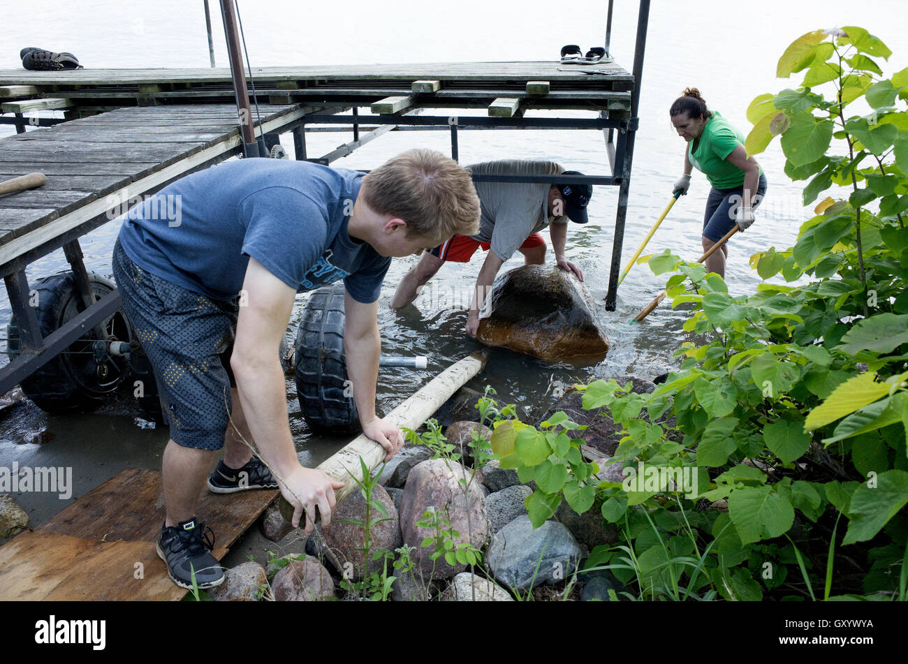 Family, mother, father and teen son moving large boulder from lakeside ...