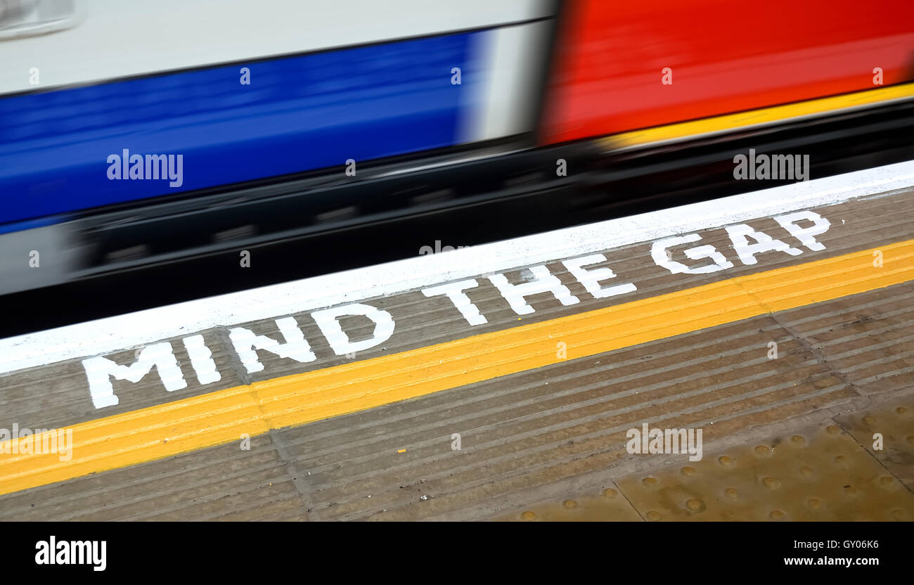 A train is going a UK platform, painted 'Mind the Gap' warning sign ...