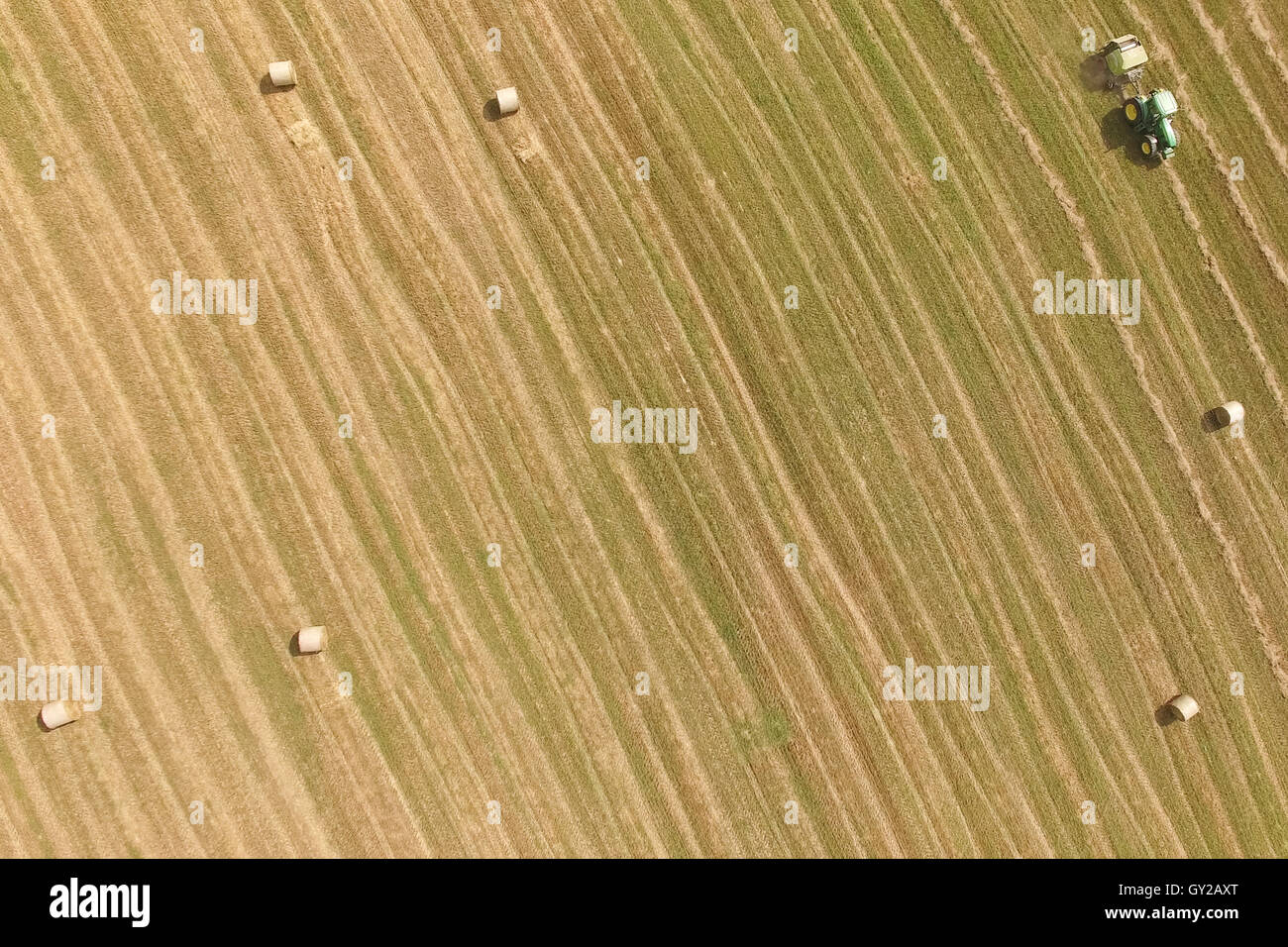 Aerial view of tractor with round baler rolling bales of straw on ...