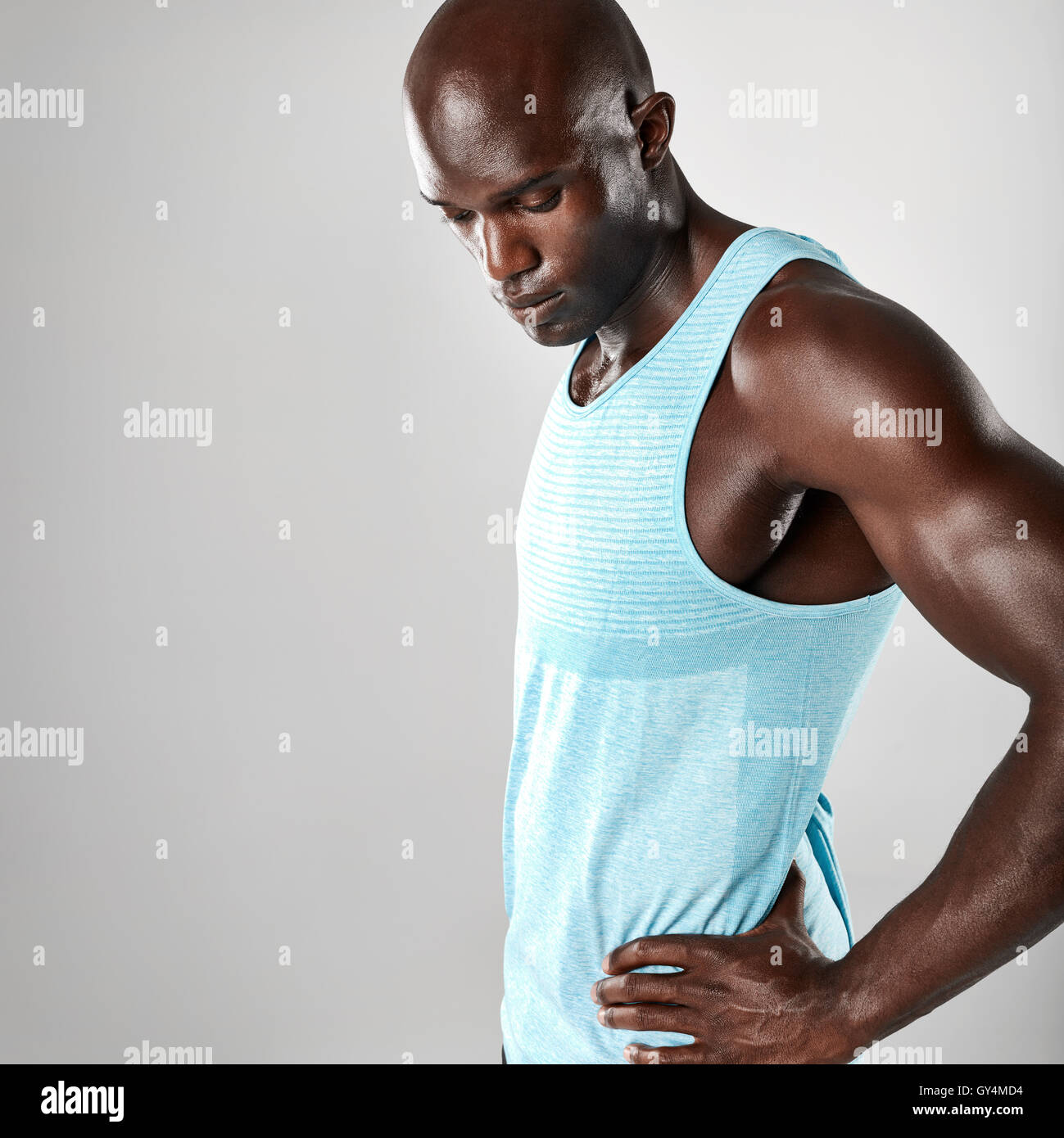 Fit young african man with muscular build looking down over grey ...