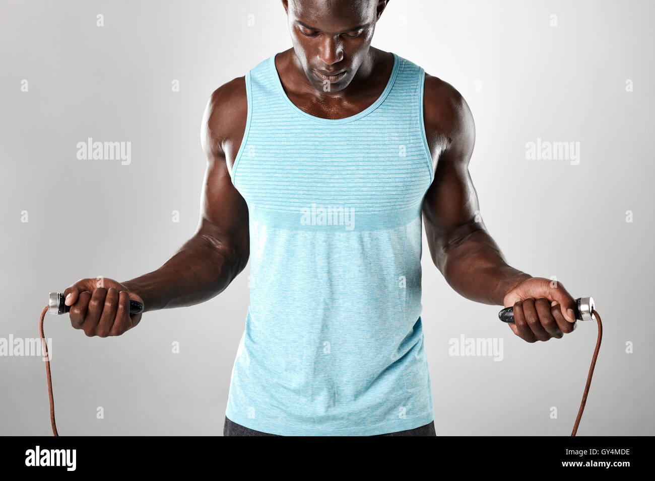 Shot of muscular young man exercising with jumping rope on grey ...