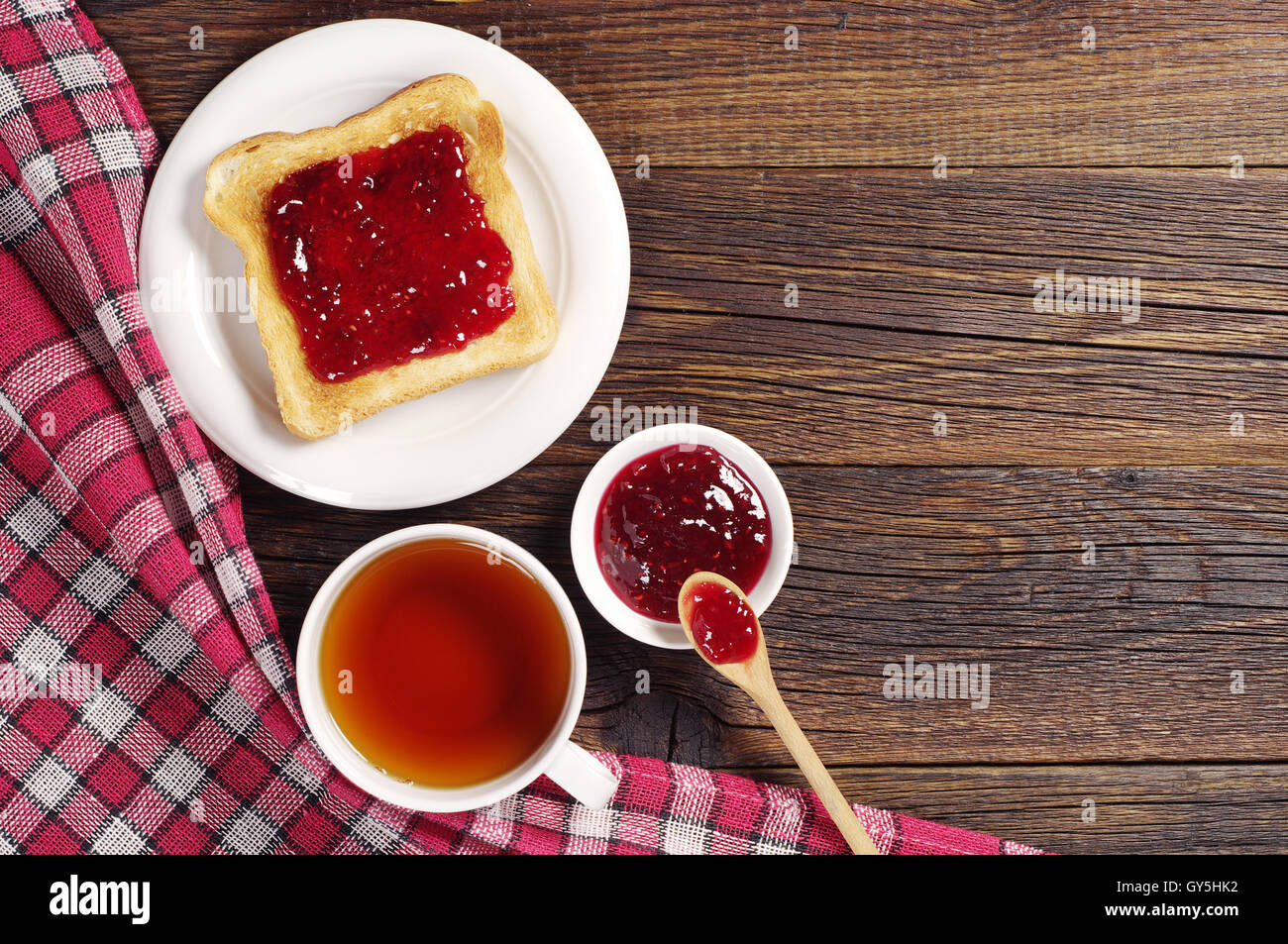 Cup of tea and toast with raspberry jam on old wooden table. Top view ...