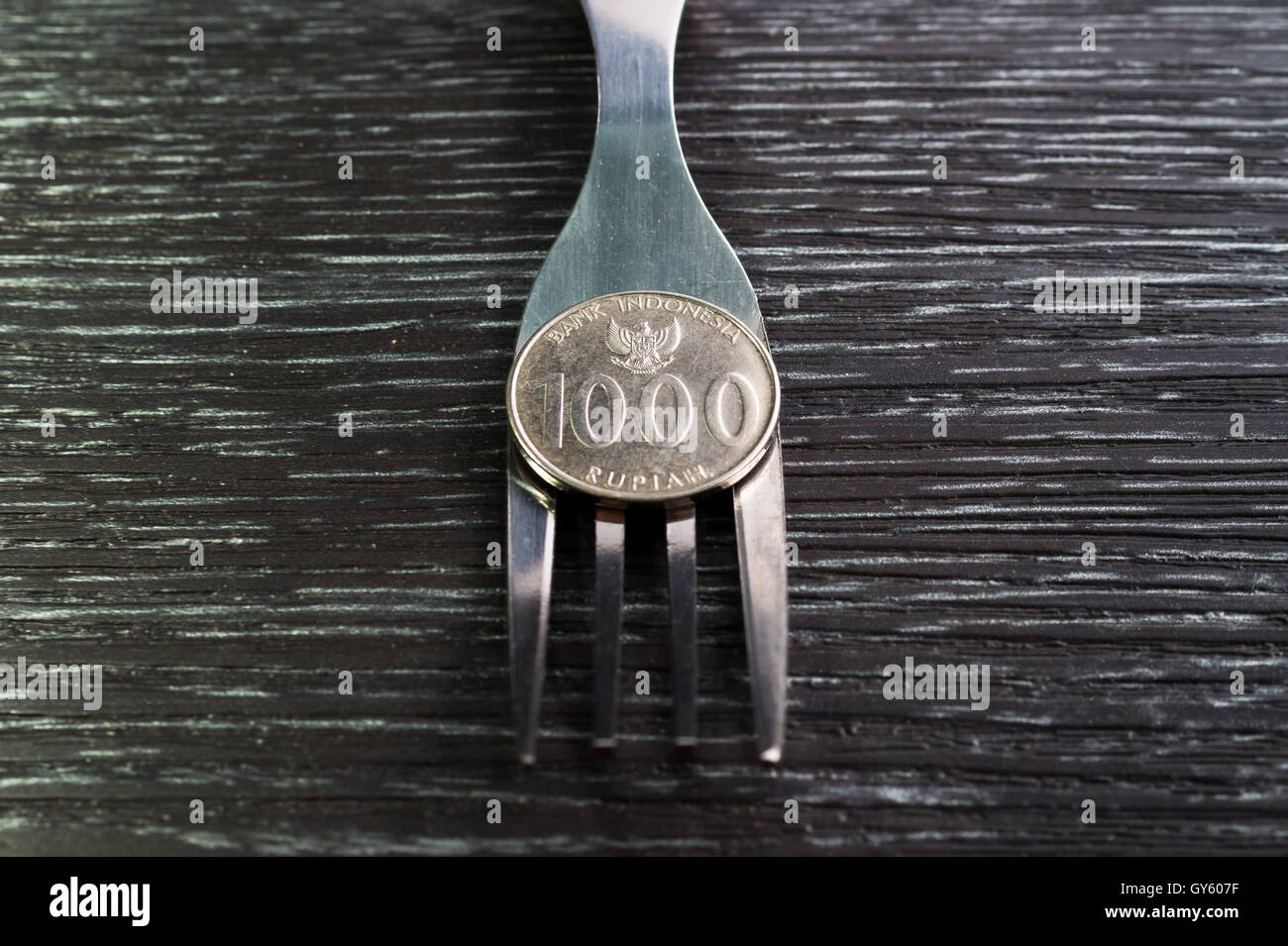 Rupiah coin on fork on black wooden texture background Stock Photo - Alamy