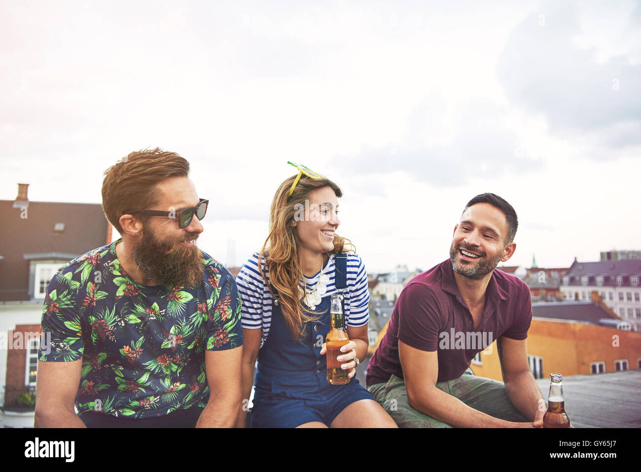 Cheerful group of young adults drinking beer from bottles on roof ...