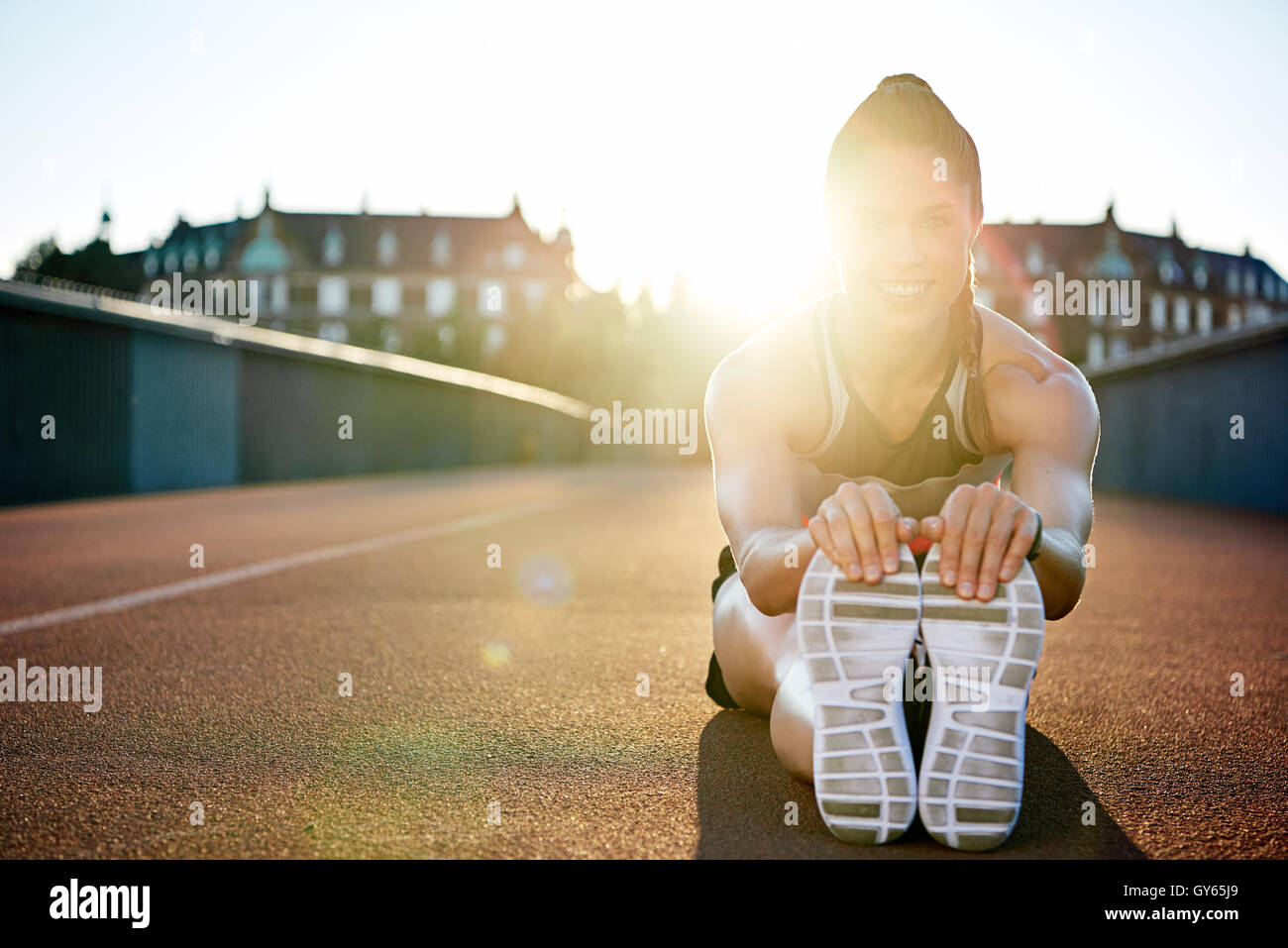Athlete limbering up before her workout sitting on a tarred bridge ...