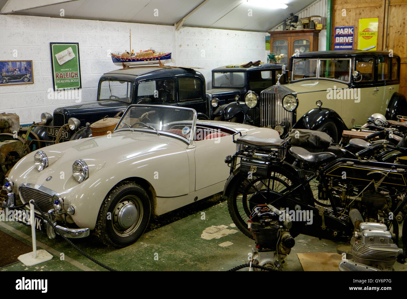 A collection of vintage cars and motorcycles are stored in a garage ...