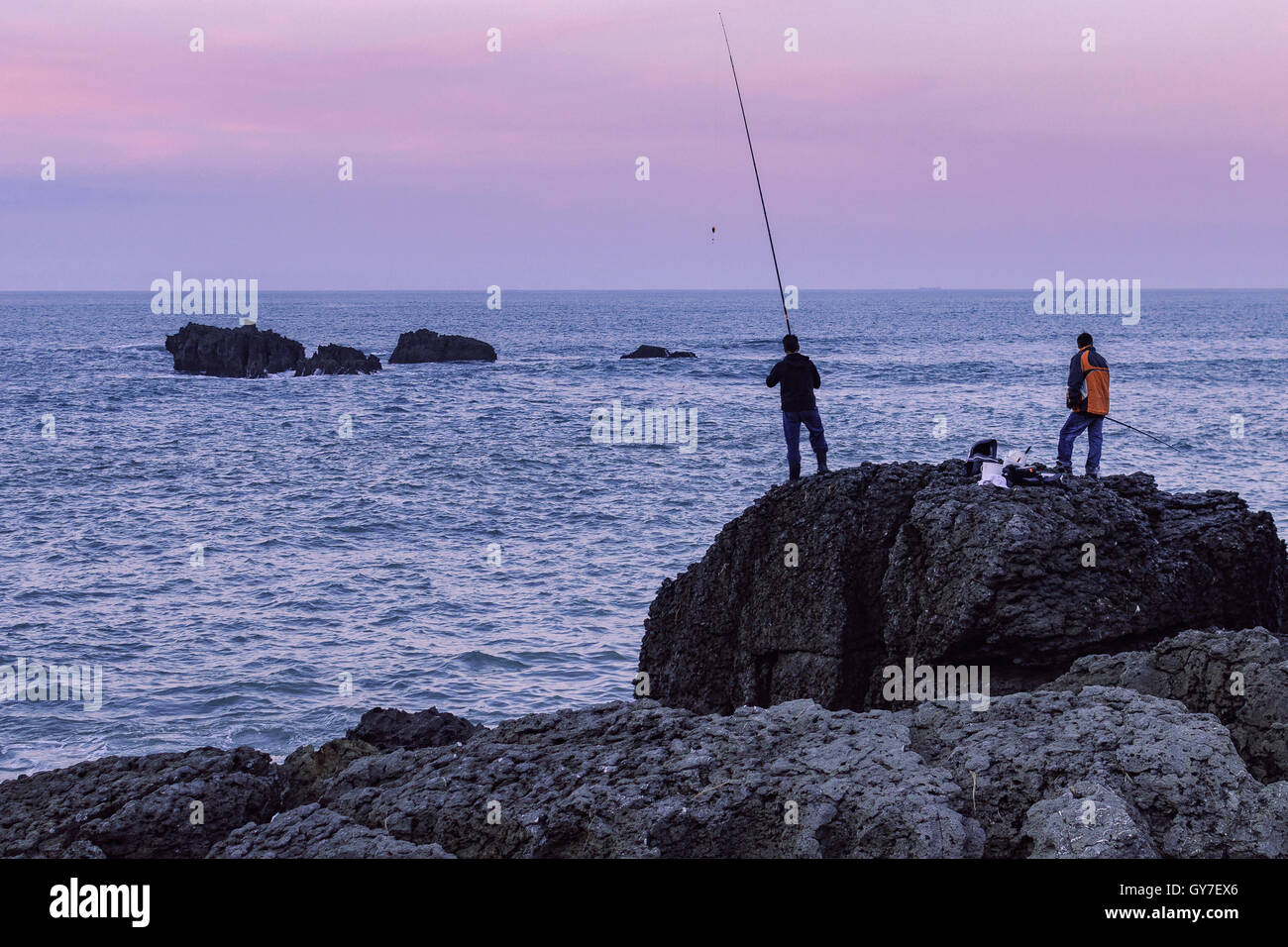 Two fishermen with their rods on the rocks, sea bottom, coastal in ...