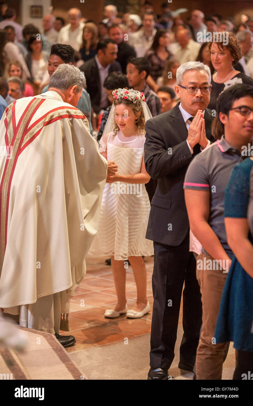 A formally dressed girl receives communion at First Communion mass at a ...