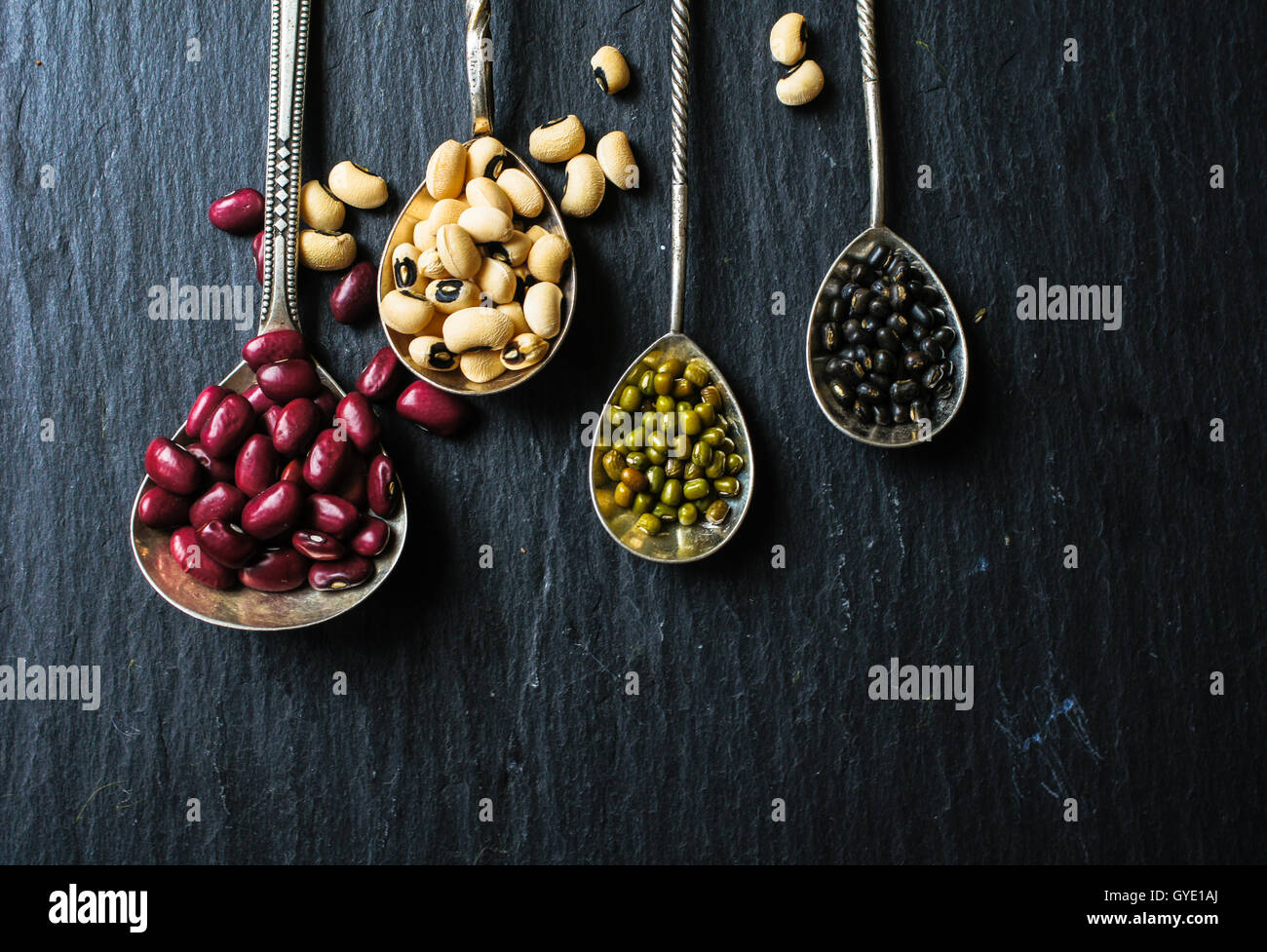 Different types of beans in the vintage spoons on the black stone ...