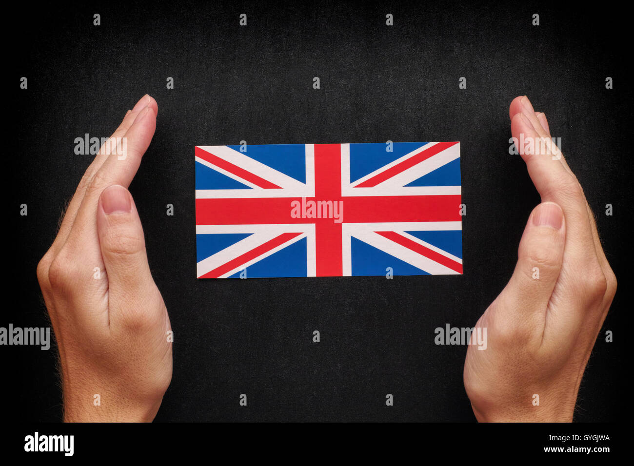 Hands protecting British Flag on black chalkboard background. Close up ...