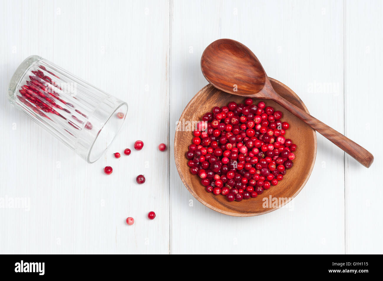 Top flat view: cranberries in wooden bowl with spoon and glass on white ...