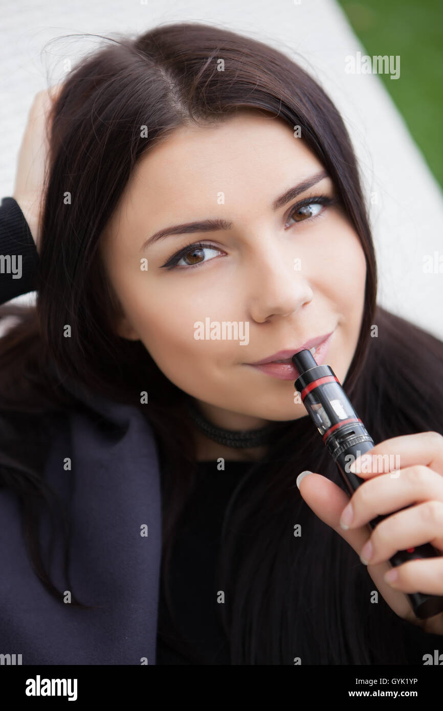 Beautiful young brunette girl vaping fruit e-liquid with very popular ...