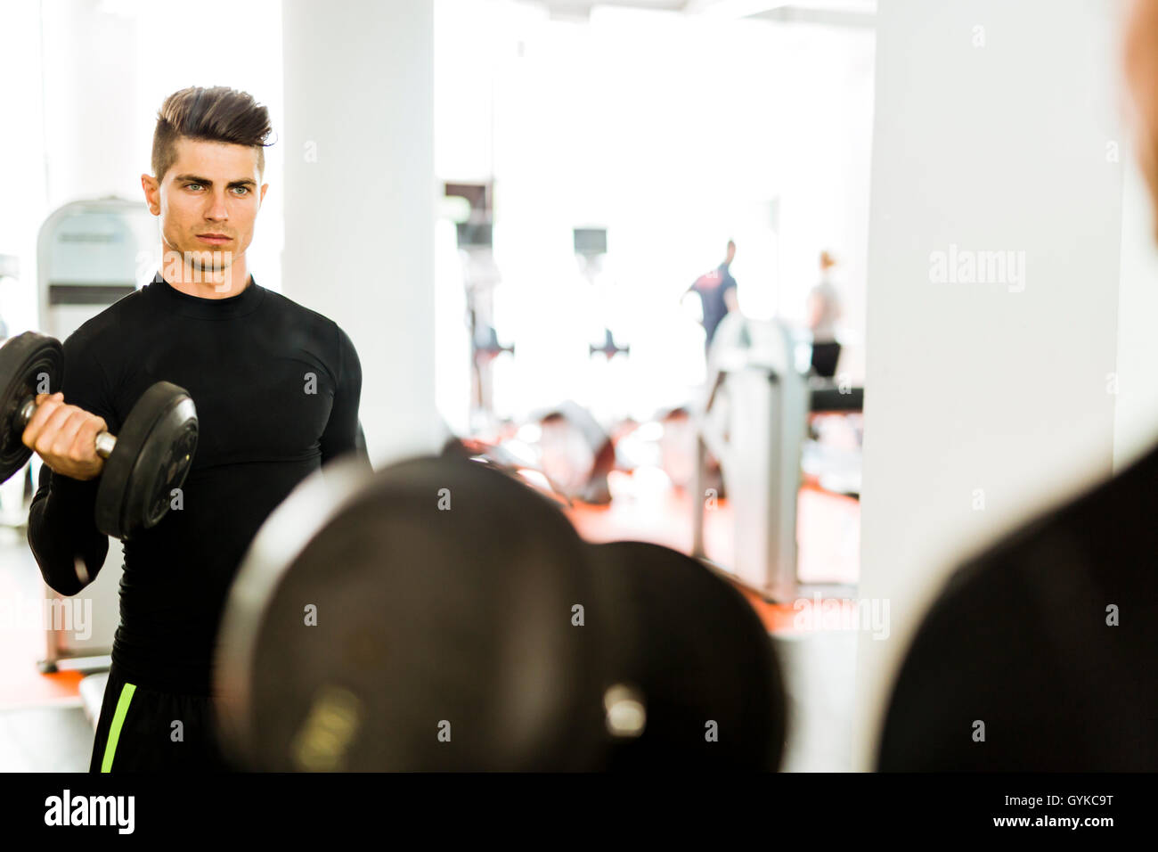 Young muscular man working out in a gym and lifting weights with his ...