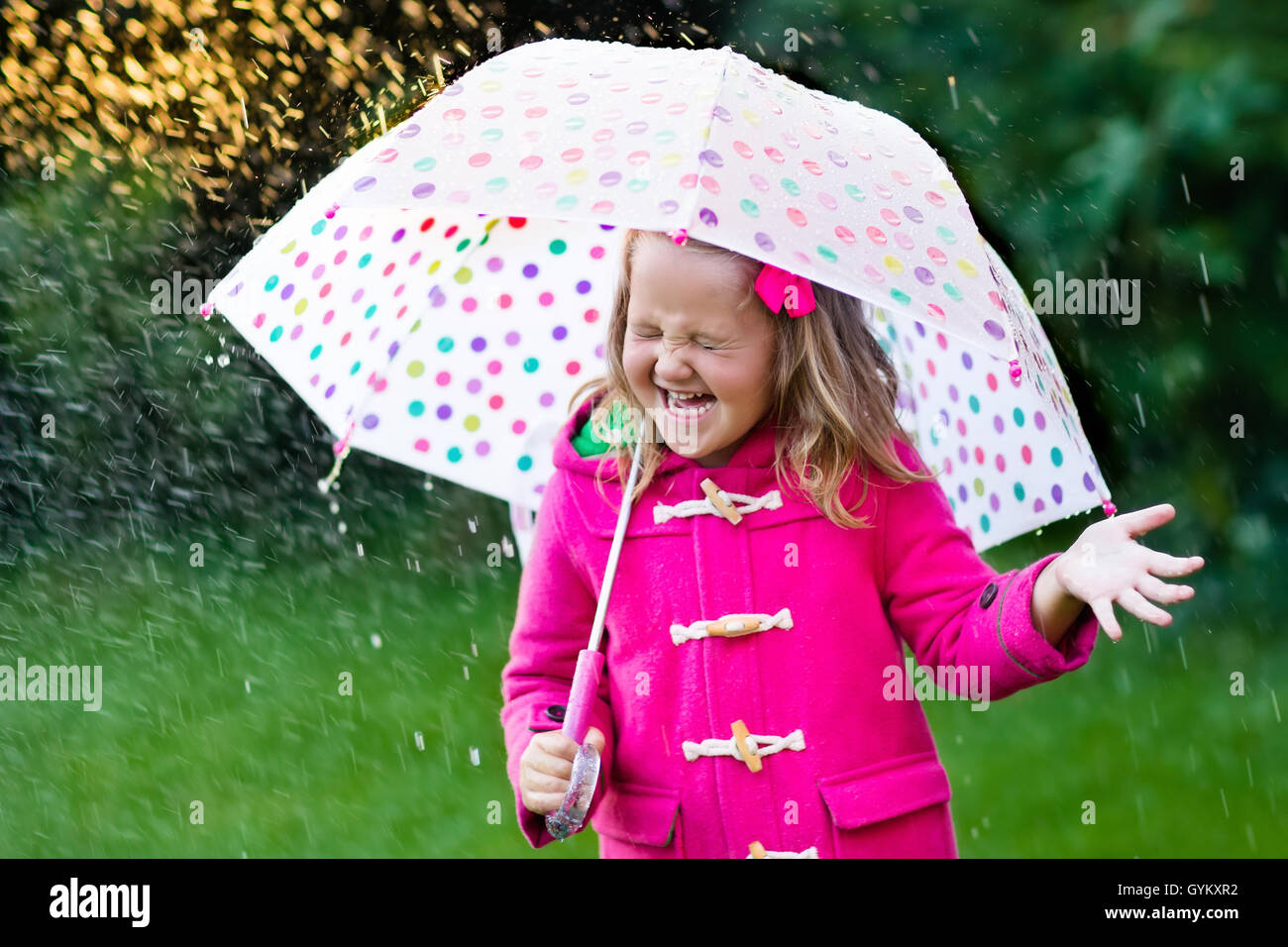 Little girl playing in rainy summer park. Child with colorful rainbow ...