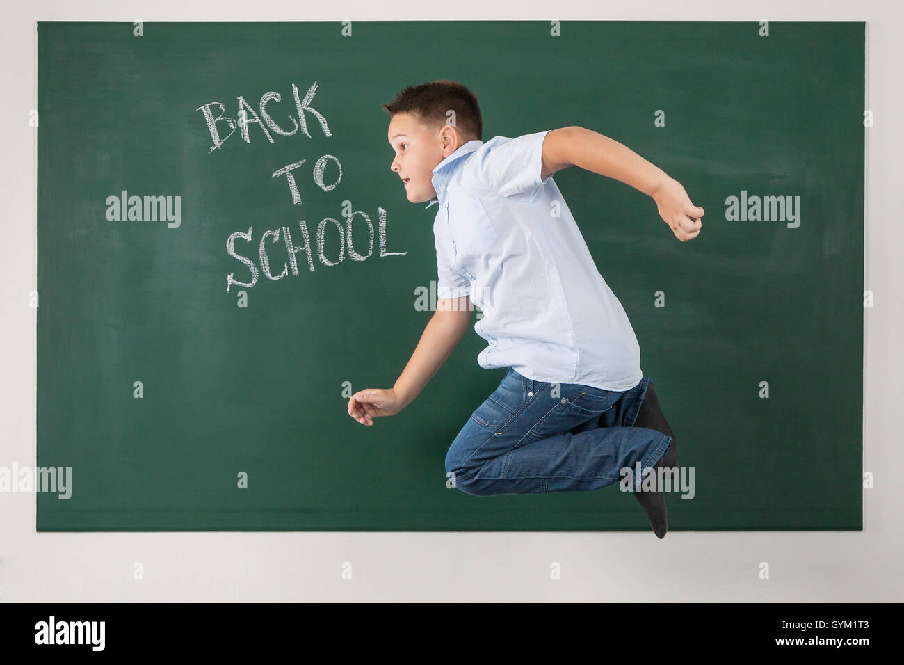 Young boy jumping in a green chalkboard with the words back to school ...