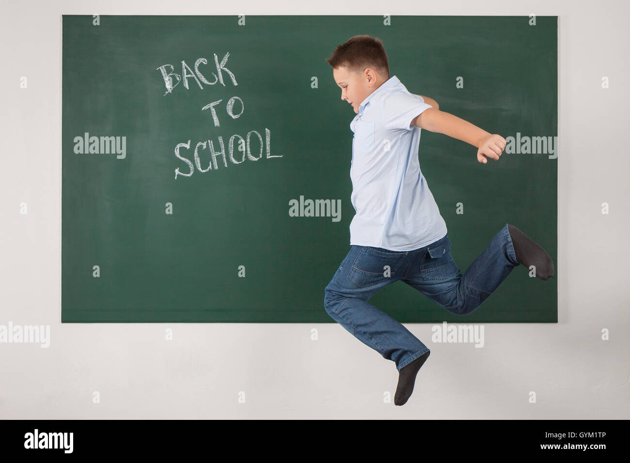 Young boy jumping in a green chalkboard with the words back to school ...