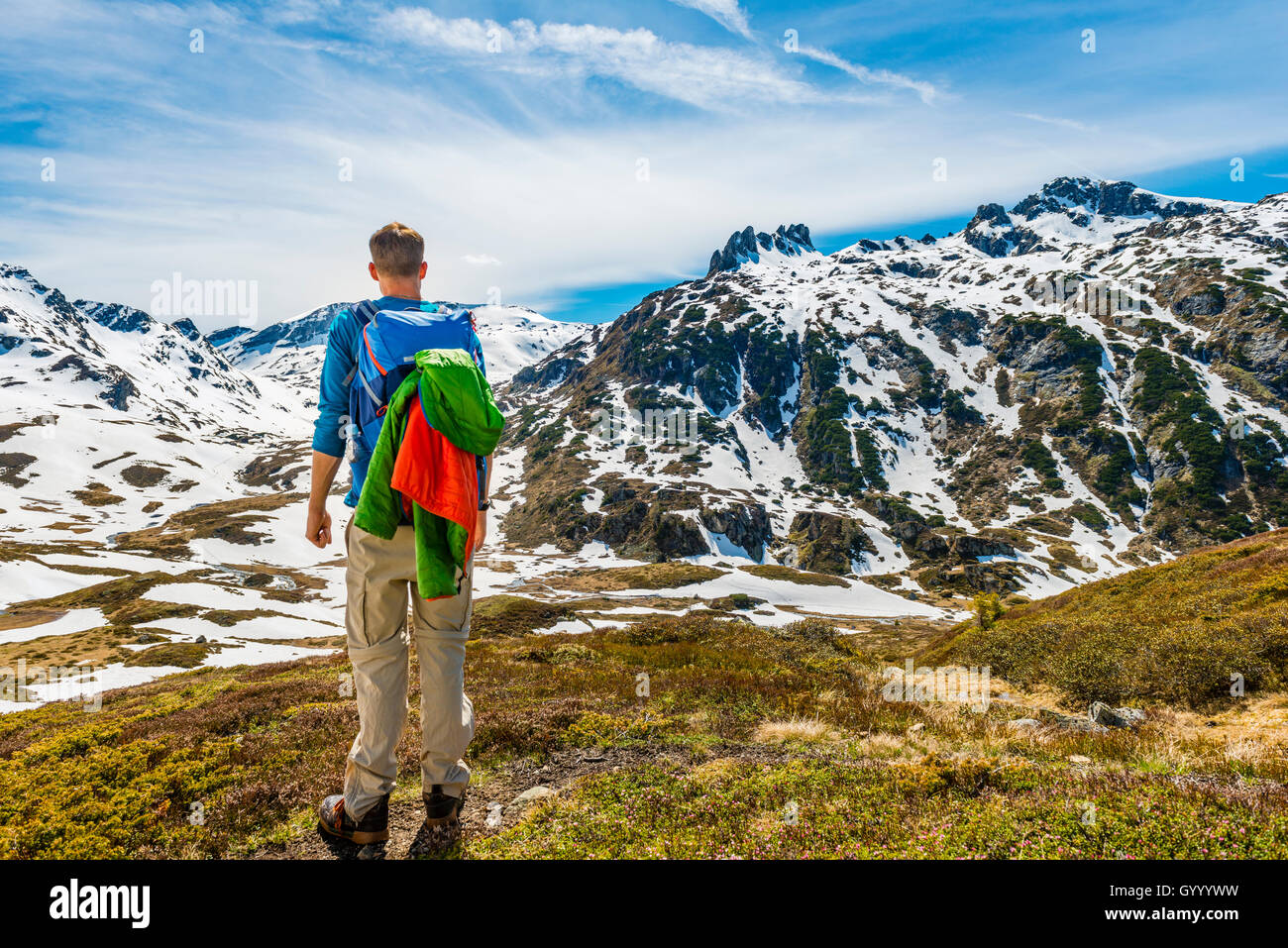 Young man hiker looks into the distance, mountain landscape, snow melts ...