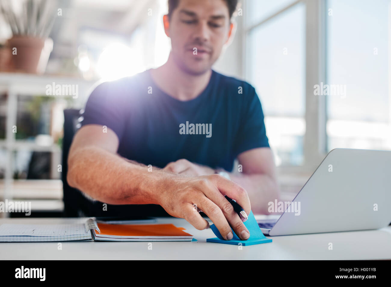 Shot of young man sitting at table and tearing a sticky post from the ...