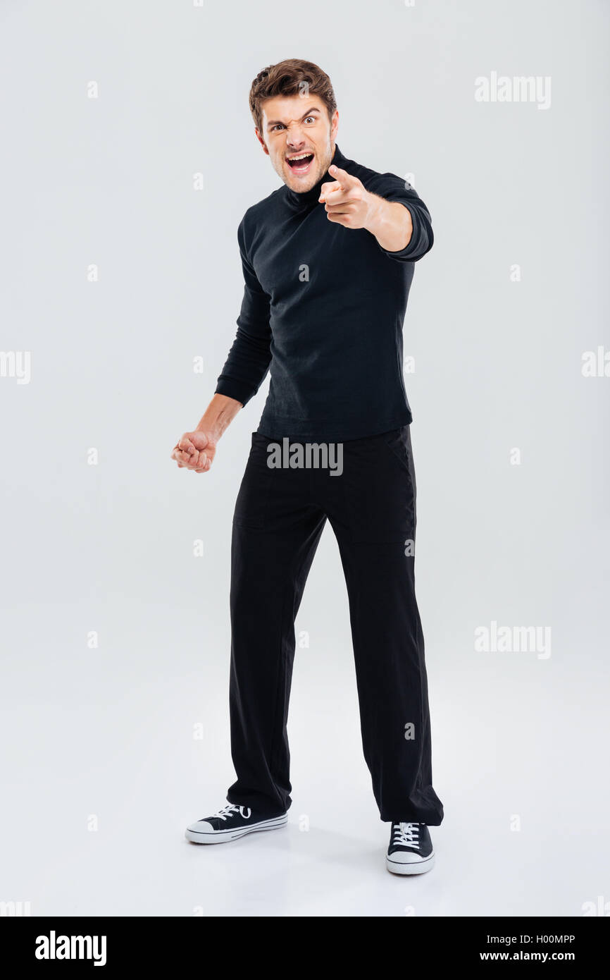 Full length of mad irritated young man shouting and pointing on you ...