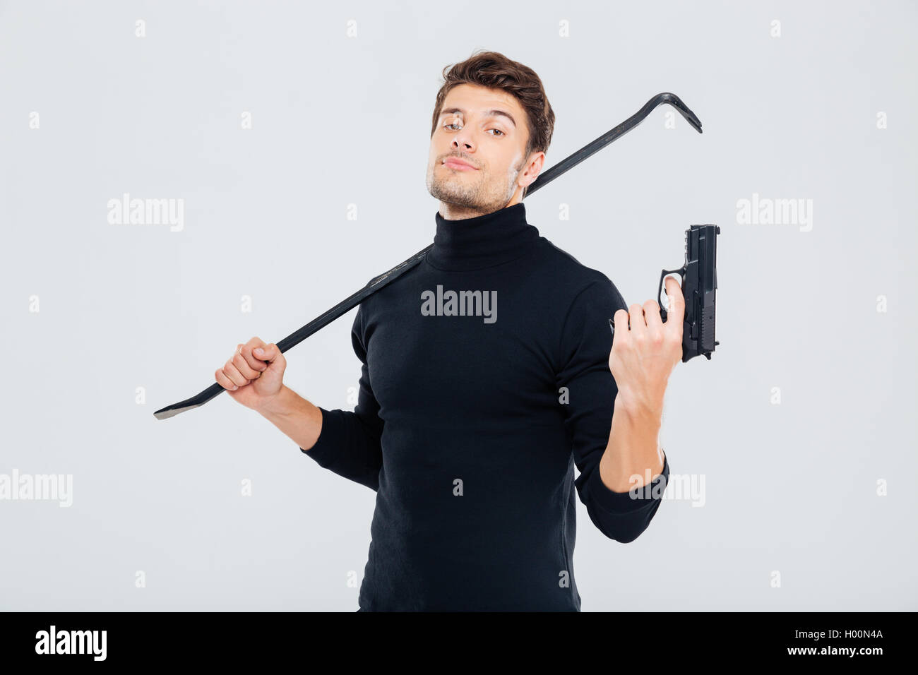 Confident young man burglar posing with gun and crowbar Stock Photo - Alamy