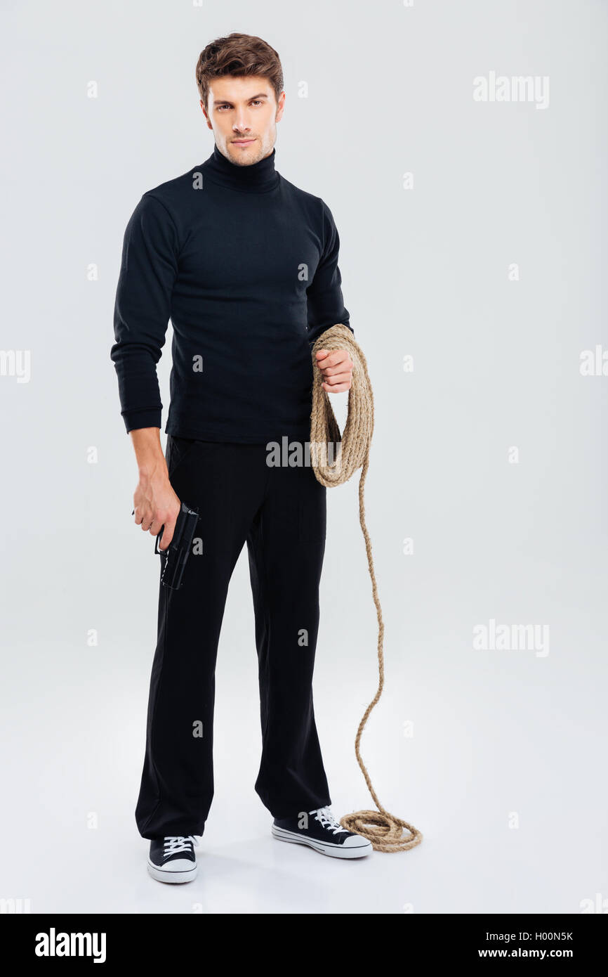 Full length of serious young man burglar with rope and gun Stock Photo ...