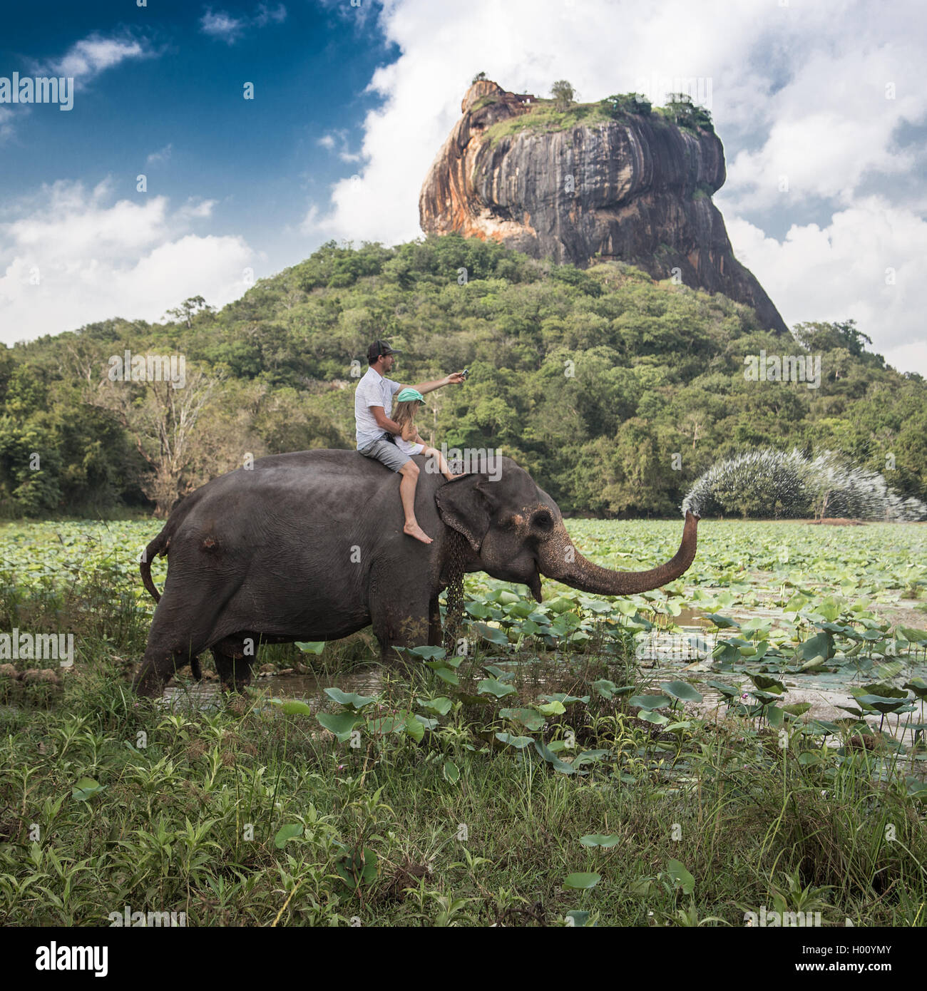 Man and child riding on the back of elephant with rock of Sigiriya as ...
