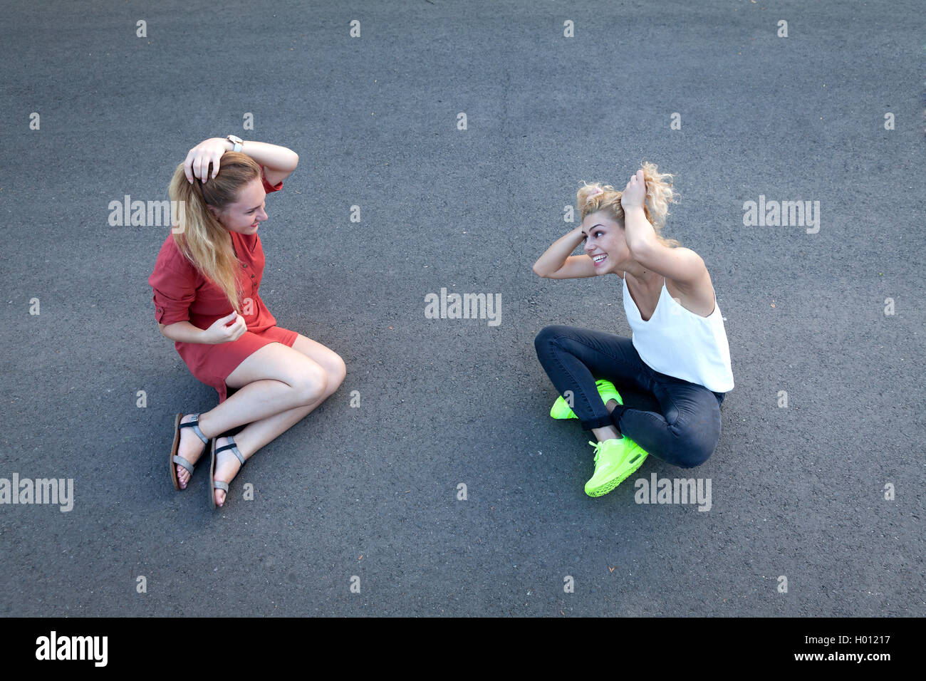Happy girls sitting on sidewalk having a chata nd making fun of it ...