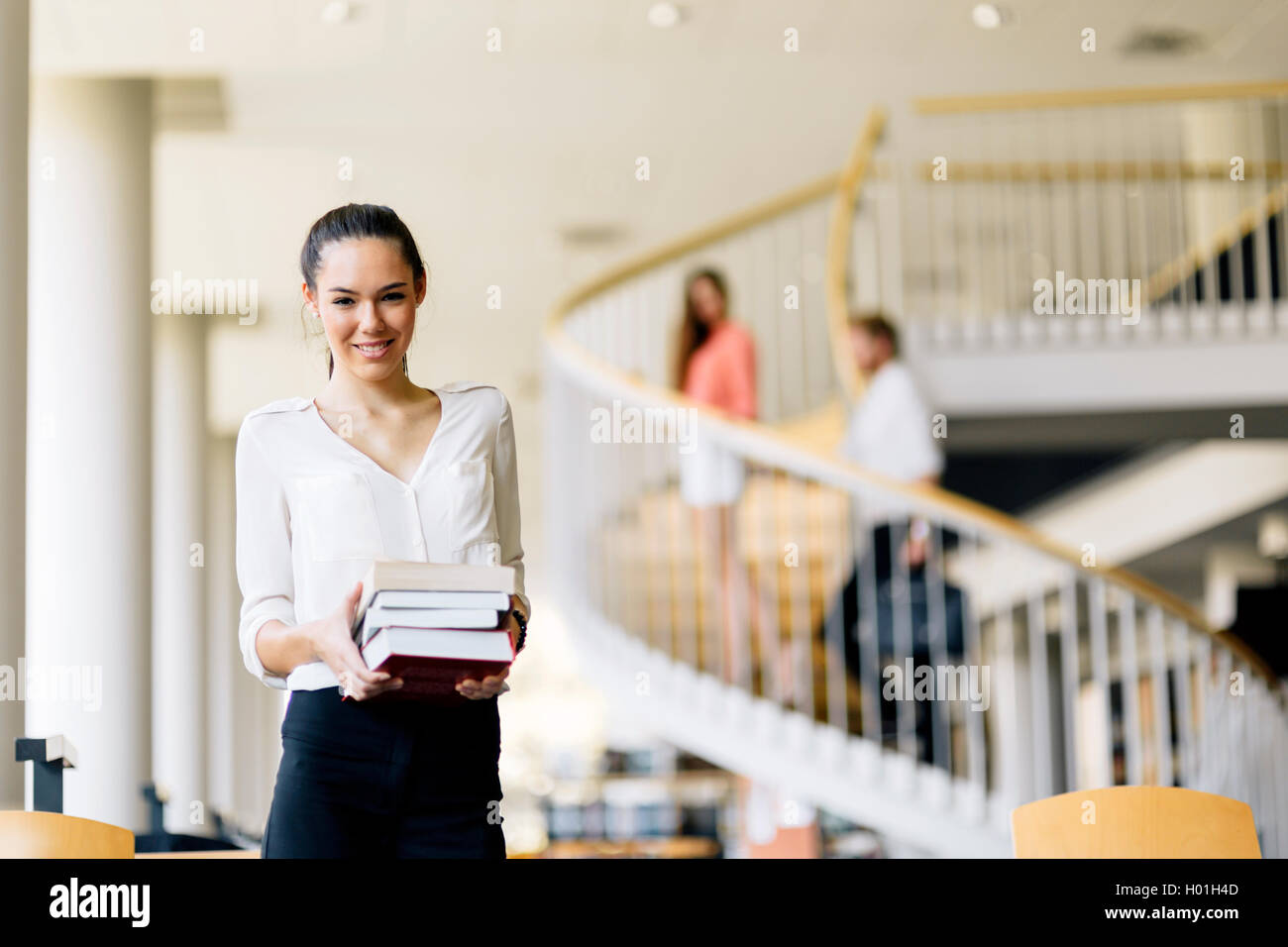 Beautiful woman holding books and smiling in a modern library Stock ...