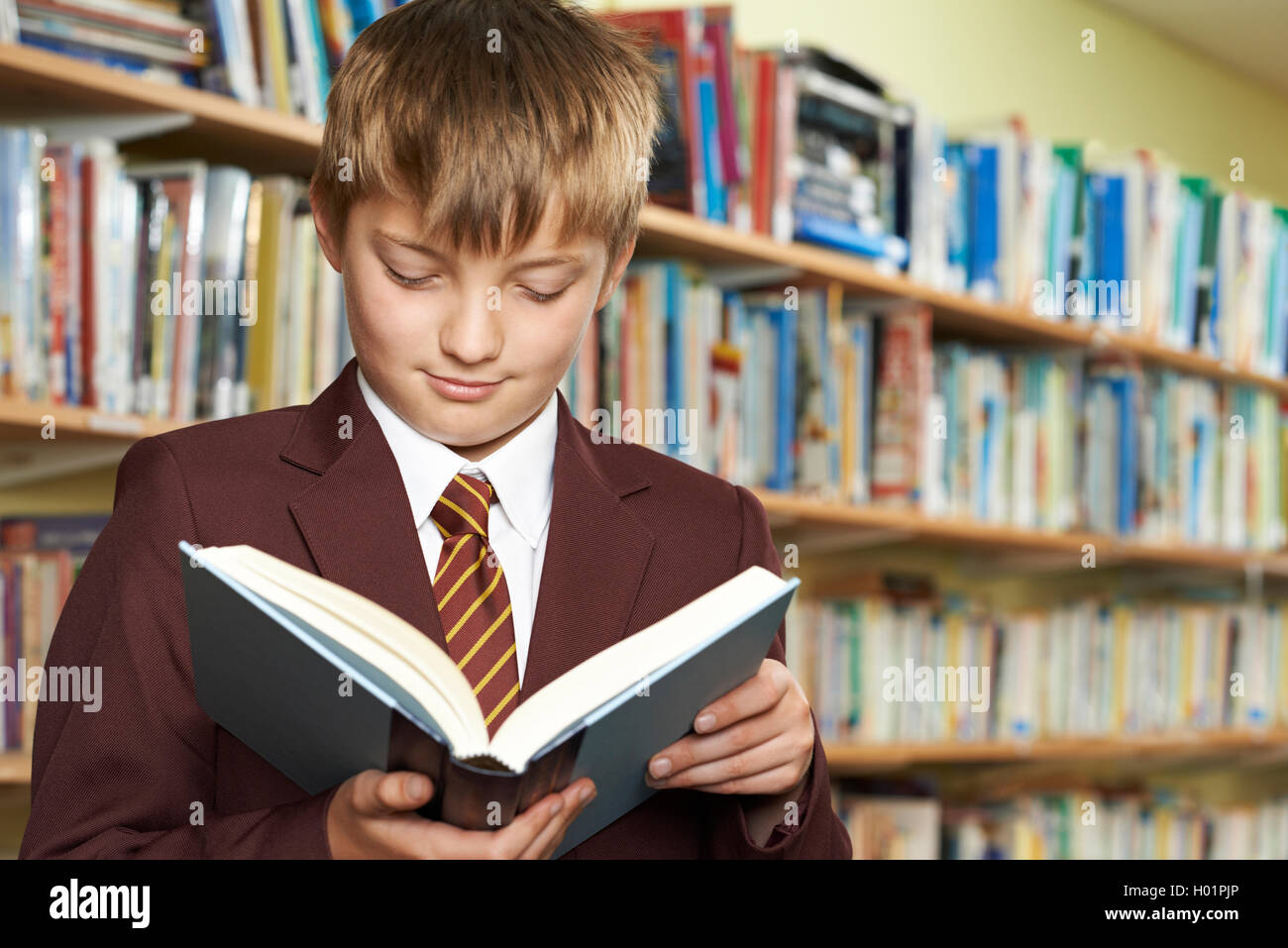 Boy Wearing School Uniform Reading Book In Library Stock Photo - Alamy