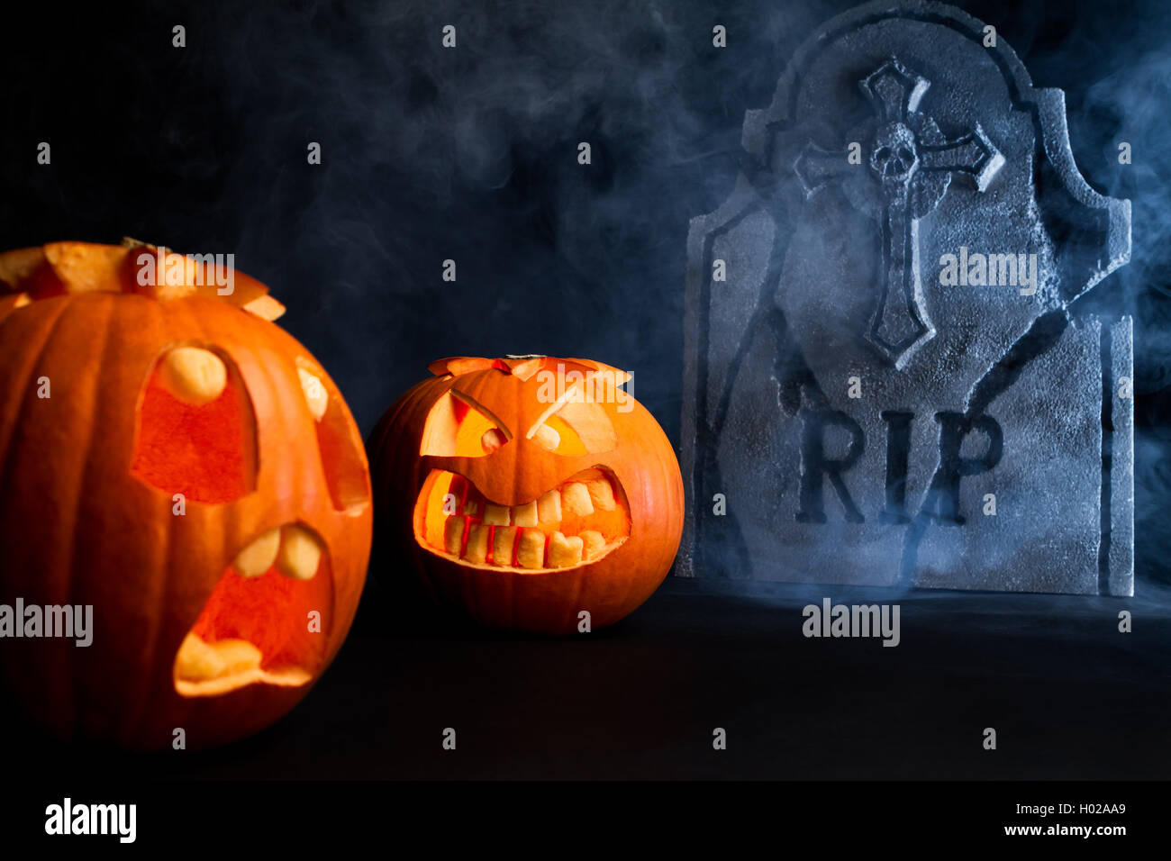 Angry face and scared face of Halloween pumpkins with tombstone on misty dark background Stock ...