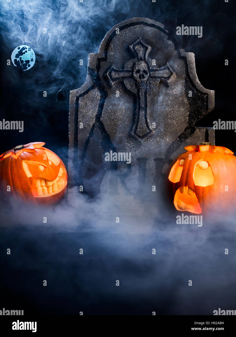 Angry face and scared face of Halloween pumpkins with moon, tombstone and bat on misty dark ...