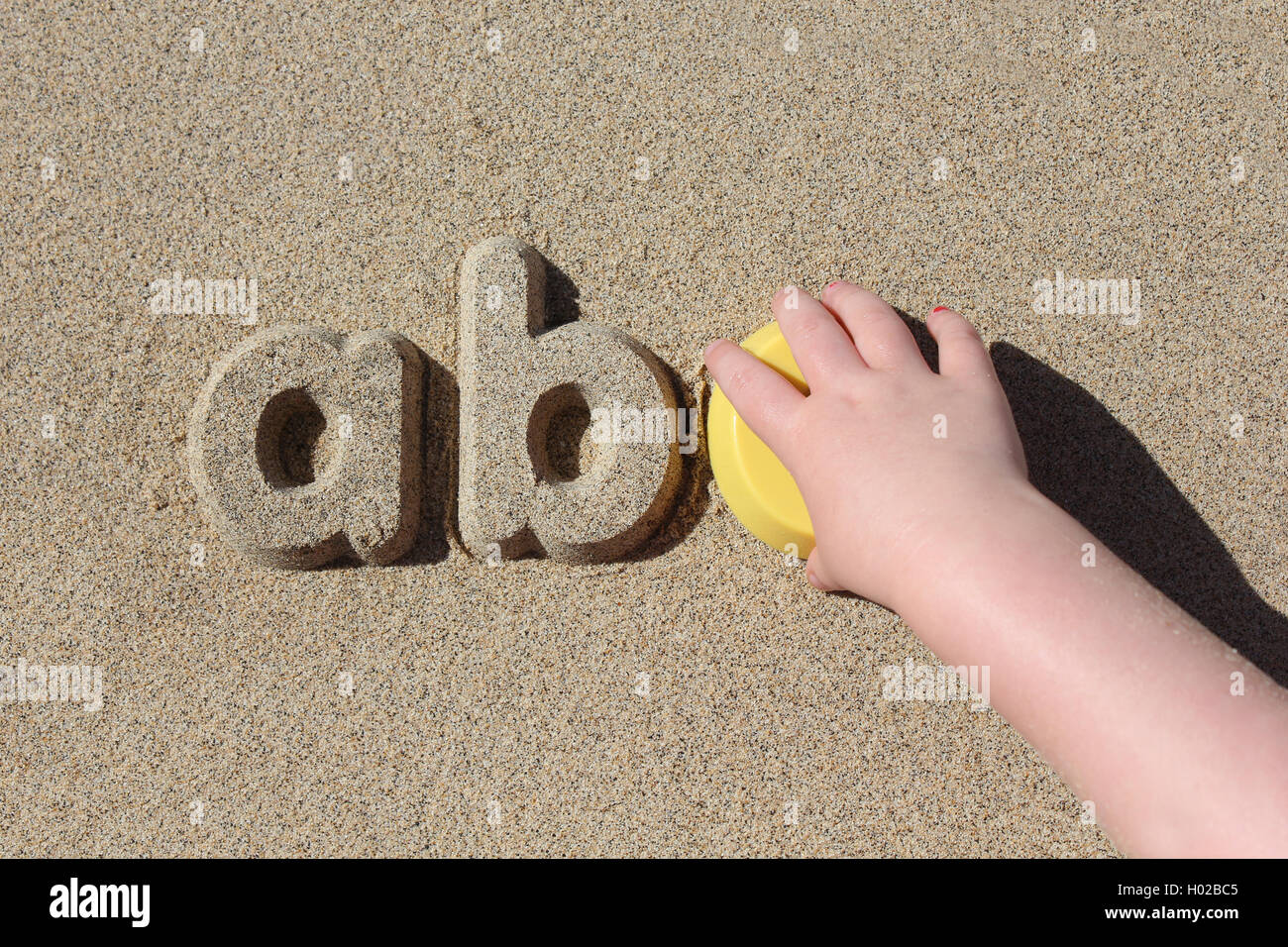 A child playing on beach. The child has made the letters 'abc' in a row ...
