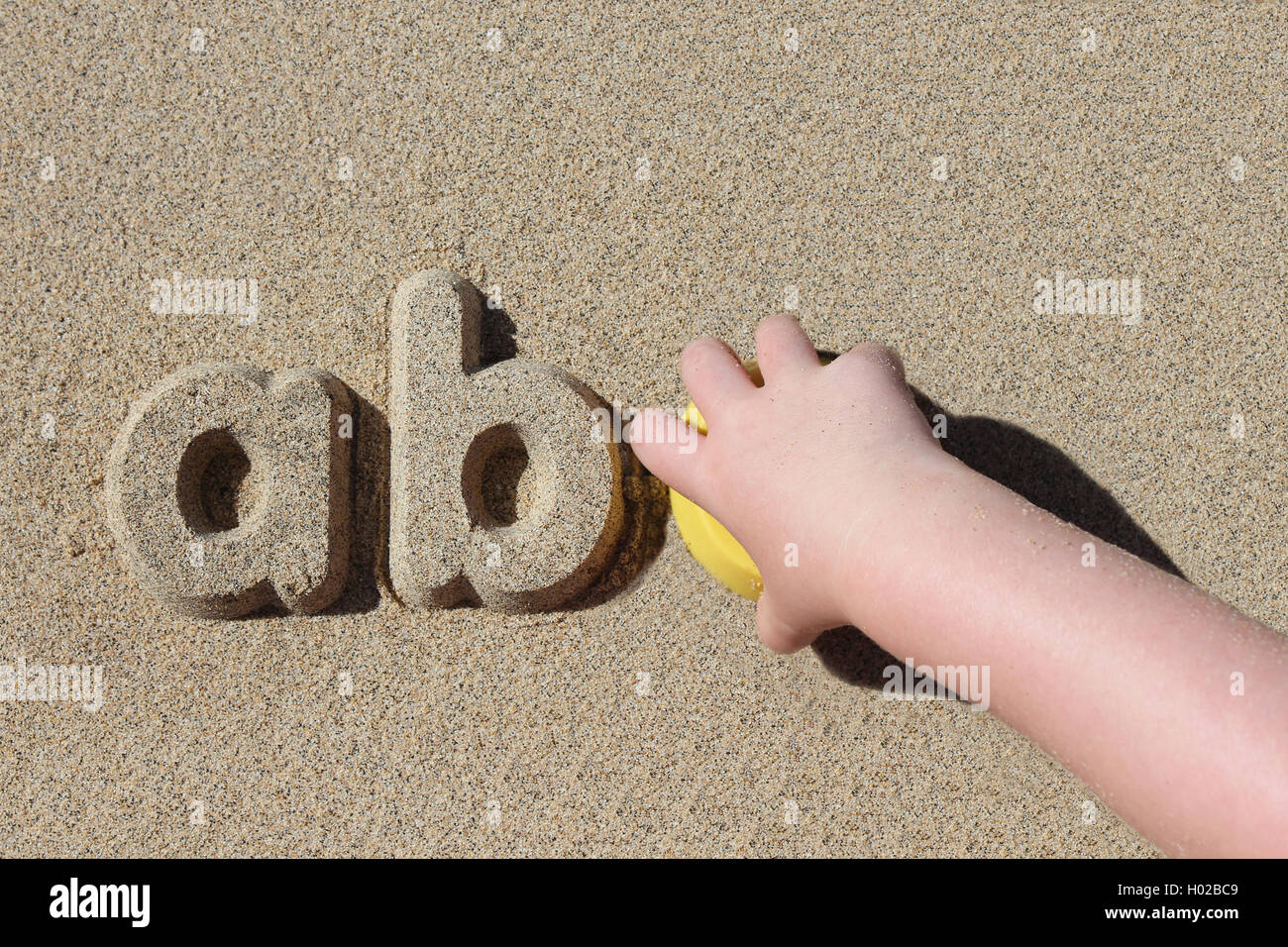 A child playing on beach. The child has made the letters 'abc' in a row ...