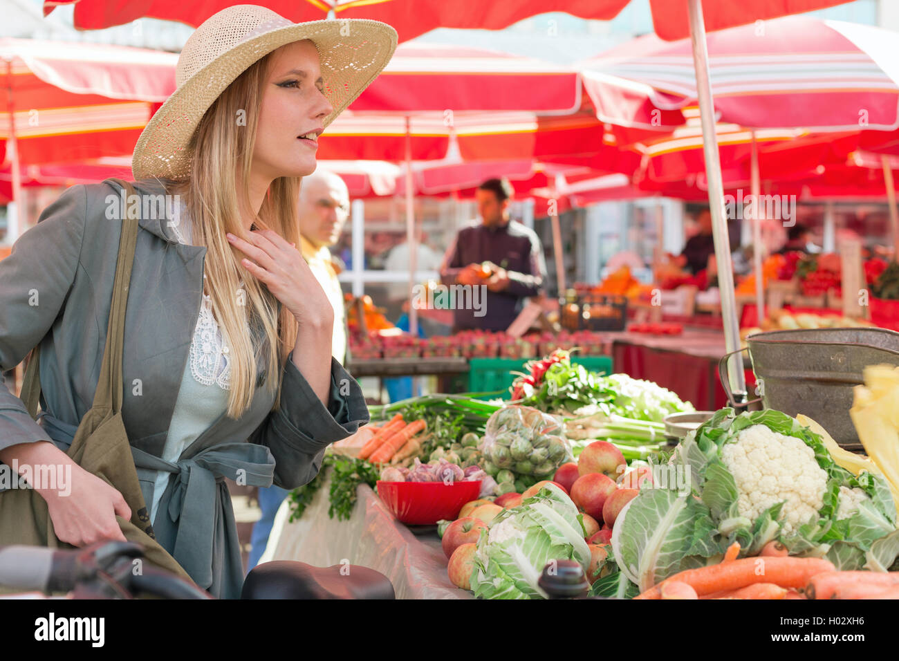 Attractive blonde girl with straw hat buying vegetables on marketplace ...