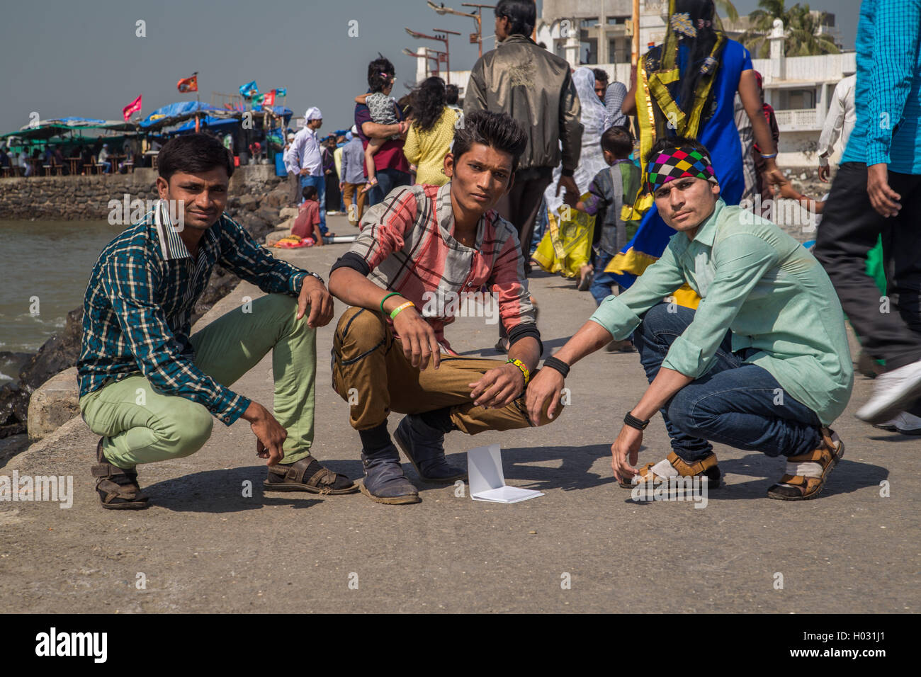 MUMBAI, INDIA - 09 JANUARY 2015: Three Indian boys crouch next to sea ...